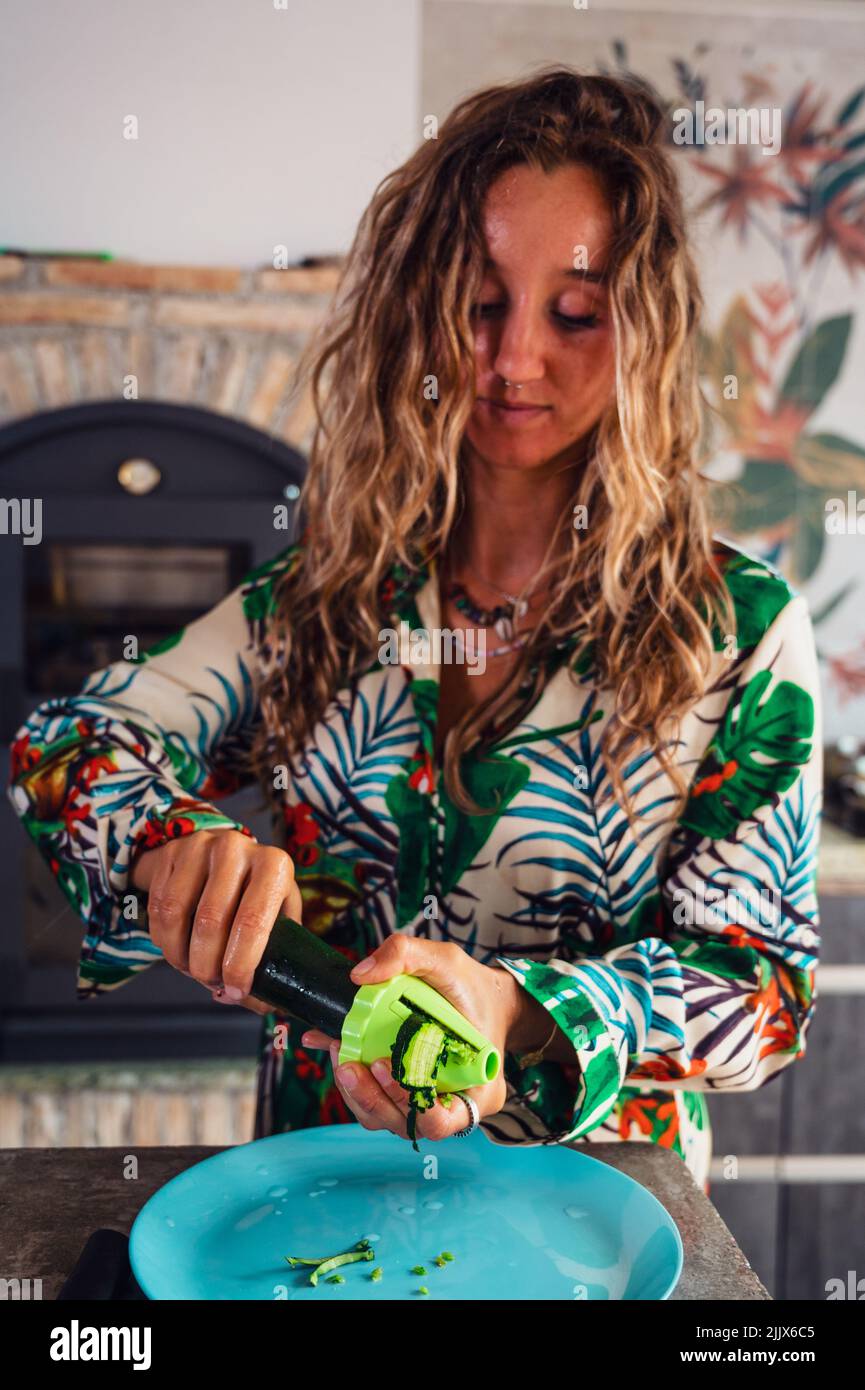 Female peeling fresh green cucumber while cooking salad in light ...