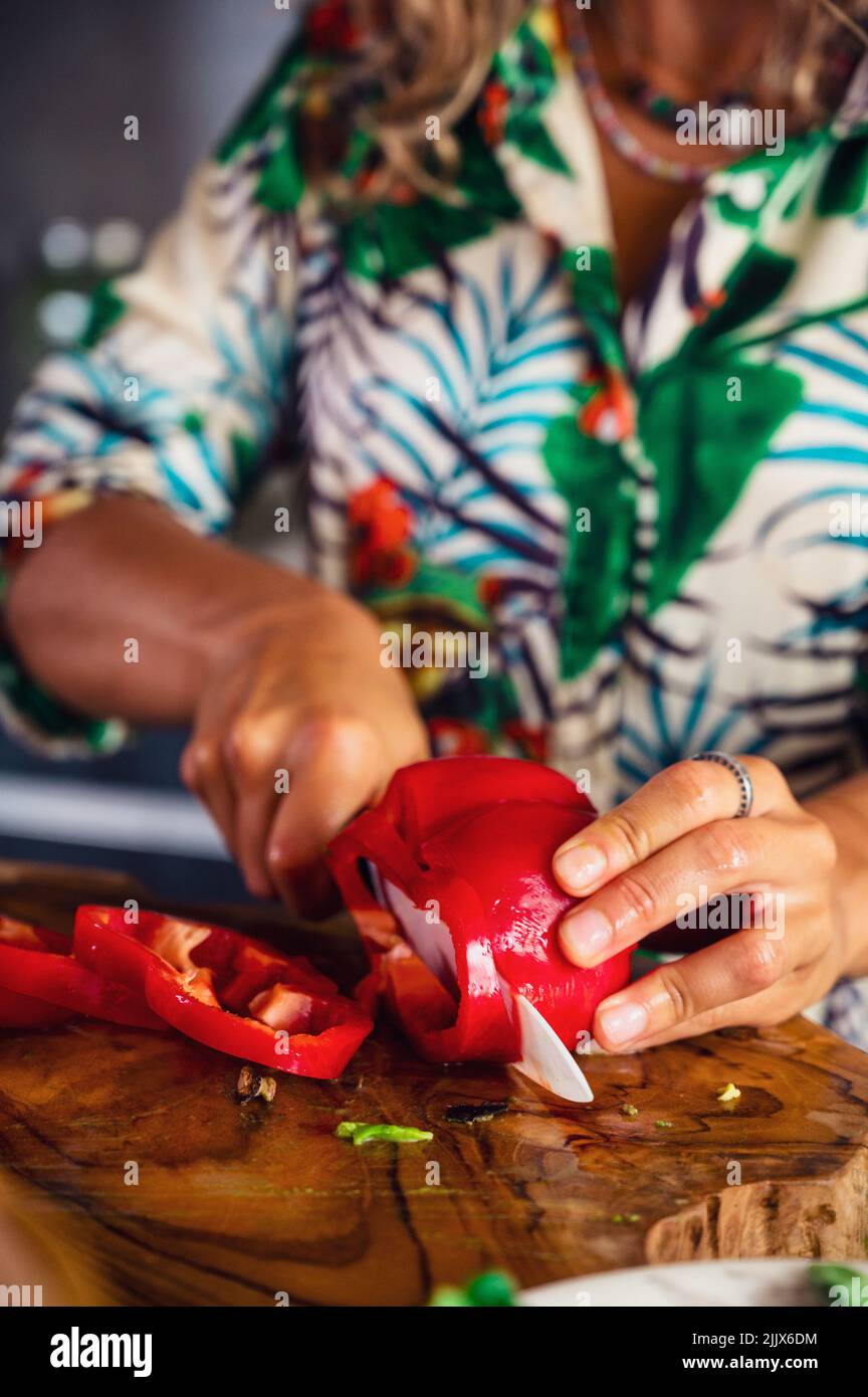 Unrecognizable female slicing red bell paper on slab of wood while ...