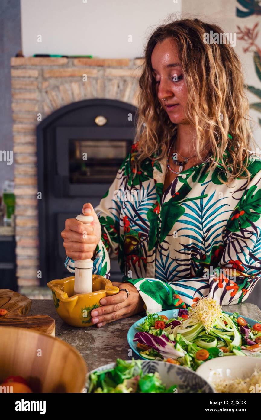 Focused female cook grinding flavorings in mortar while making healthy ...