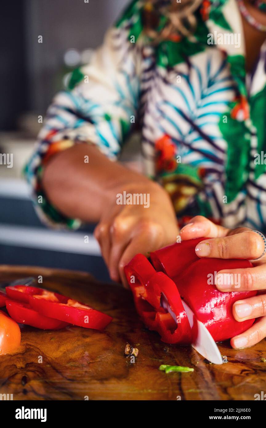 Unrecognizable female slicing red bell paper on slab of wood while ...