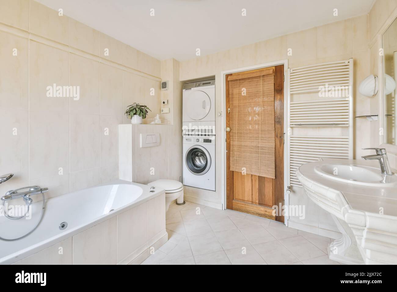 Interior of tiled bathroom with washing machine and dryer near bathtub ...