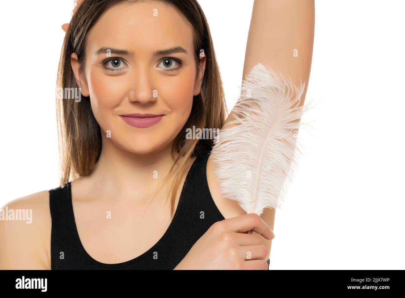 young smiling woman caressing the armpit with white feather on a white ...