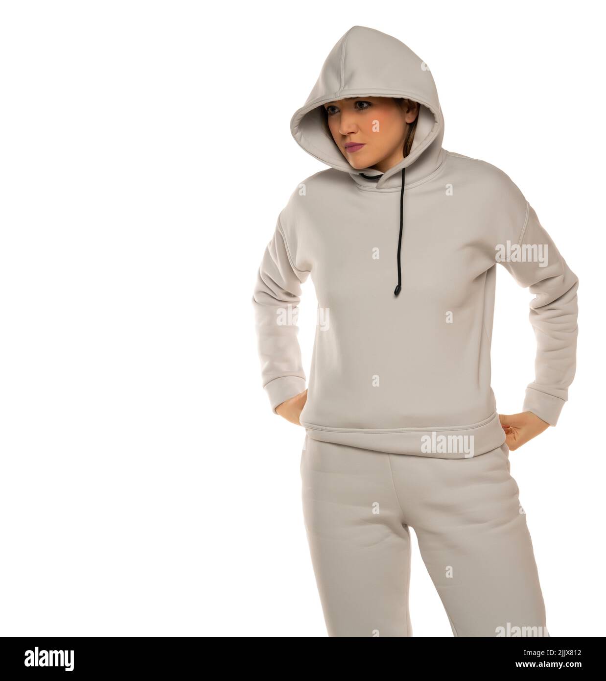 a young woman in a gray tracksuit and hood poses against a white ...