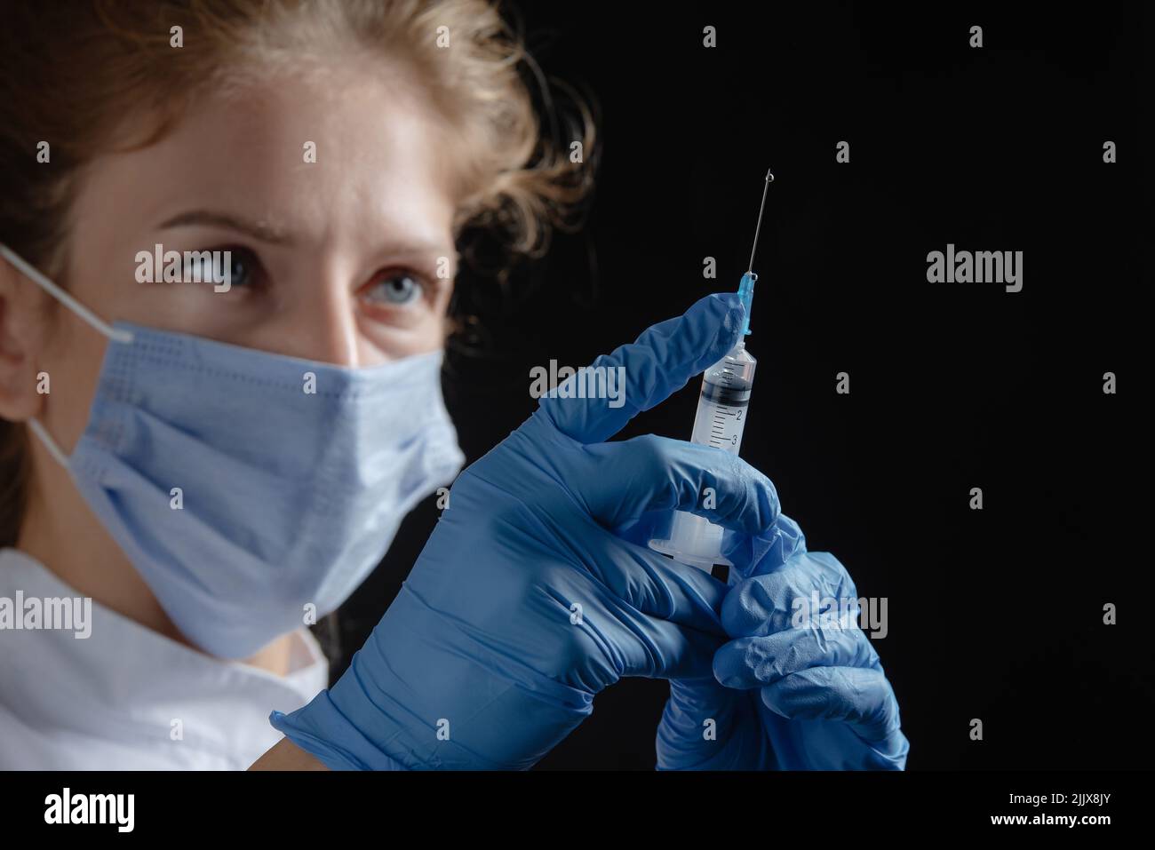 A female doctor wearing a protective mask and gloves holds a syringe ...