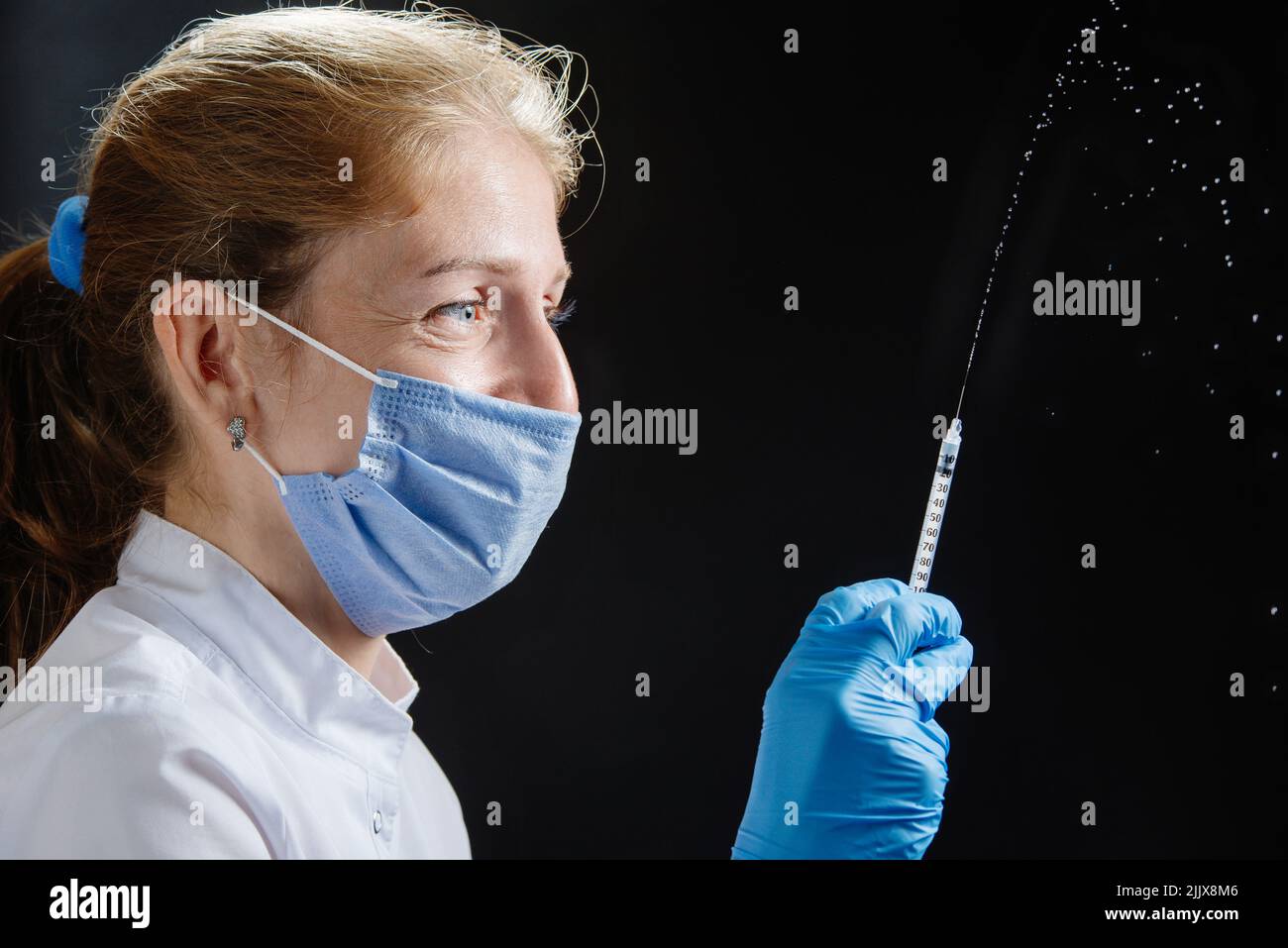 the doctor sprays from a syringe against a black background. The doctor ...