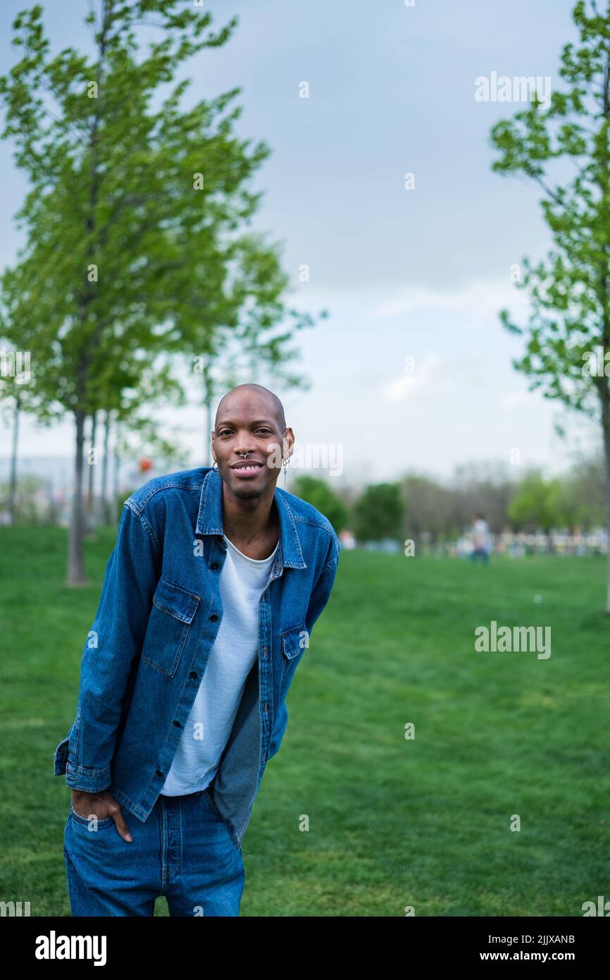 Half-length portrait of young non-binary man in park outdoors smiling ...