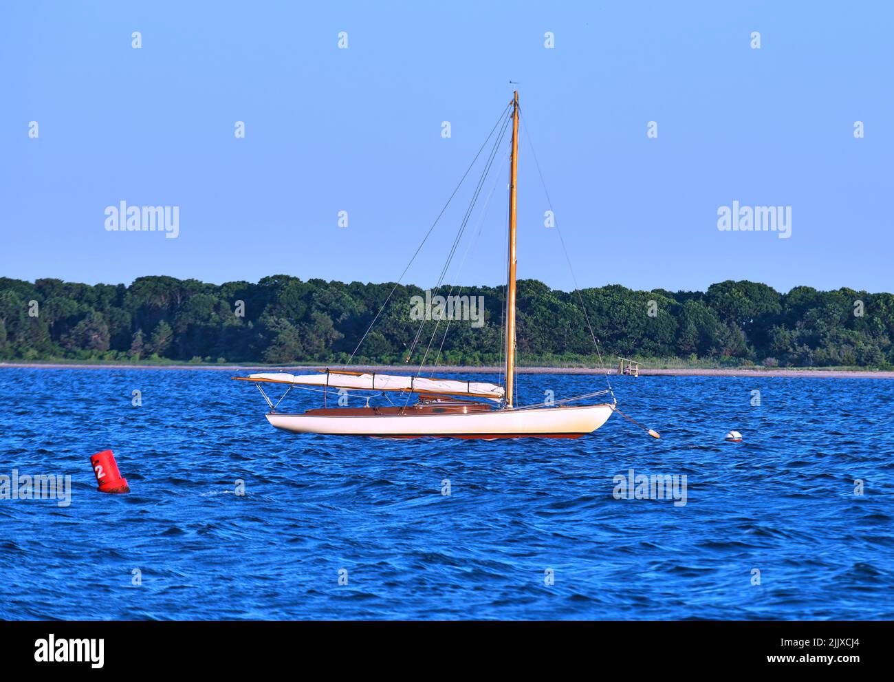 A wooden Sail boat and red buoy with sails down and anchored in a ...