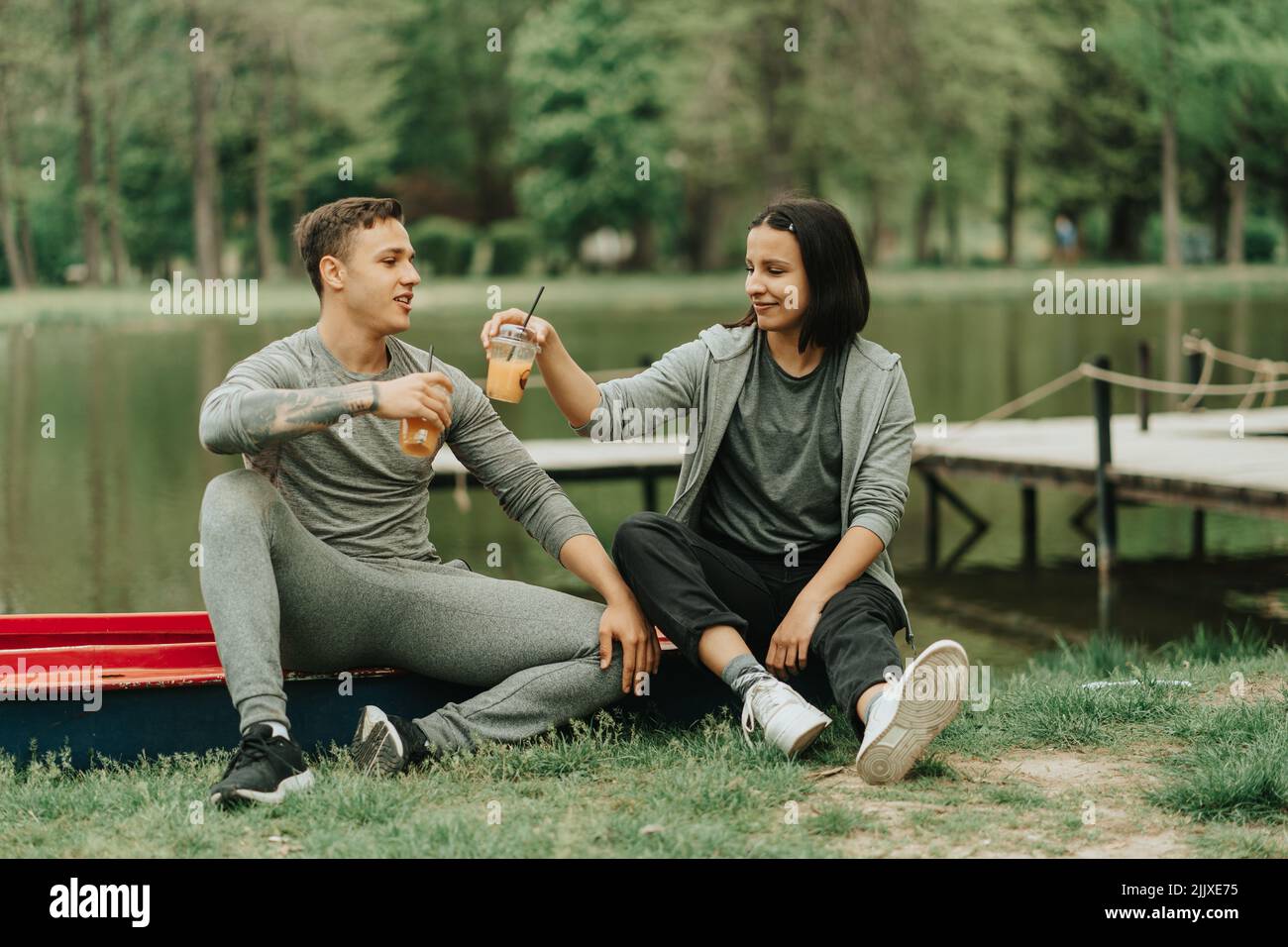 Pretty couple drinking juices while sitting on a red kayak in the park ...