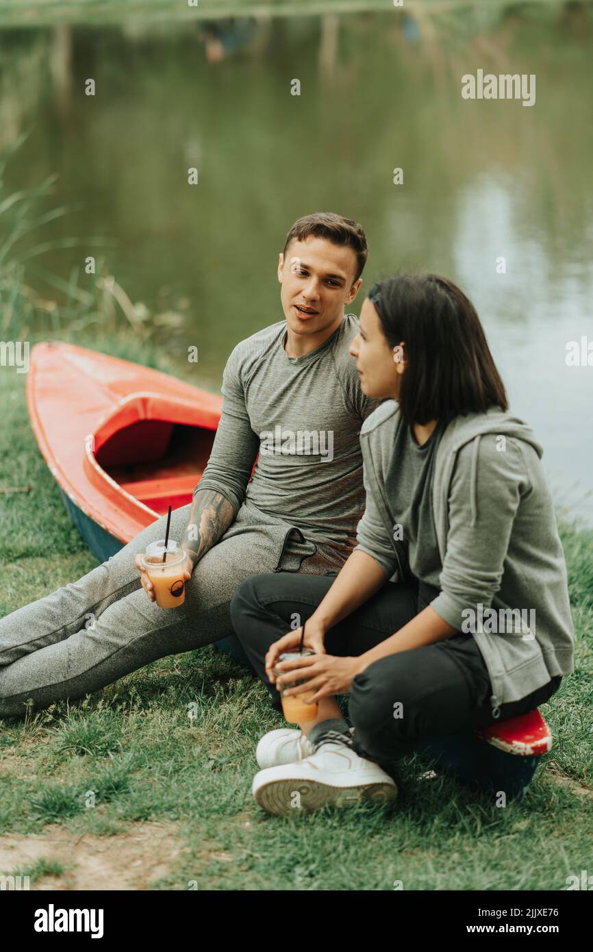Amazing couple talking while sitting on a kayak in the park drinking ...