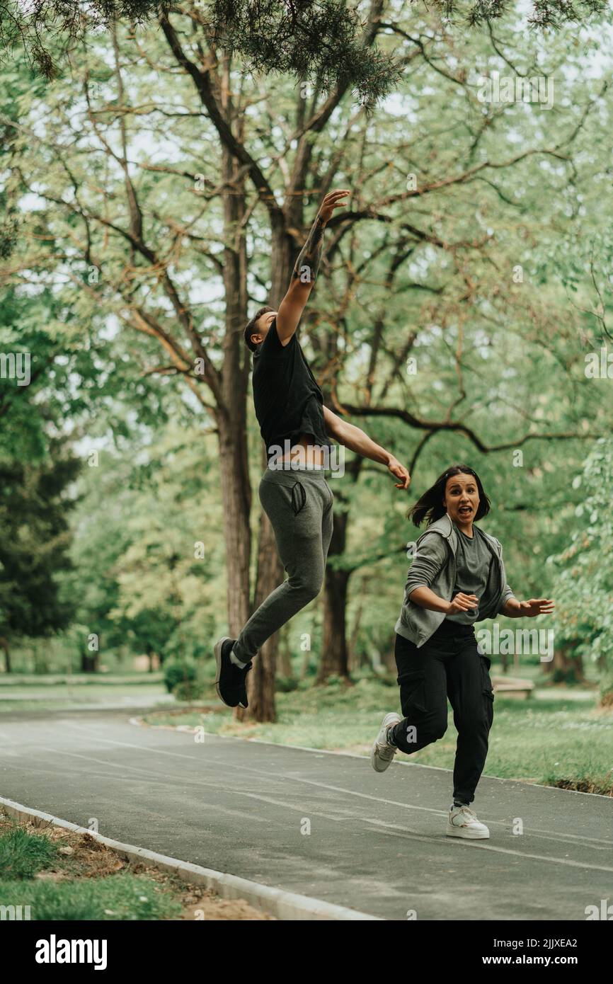 Beautiful couple jumping on the silver path while running in the park ...