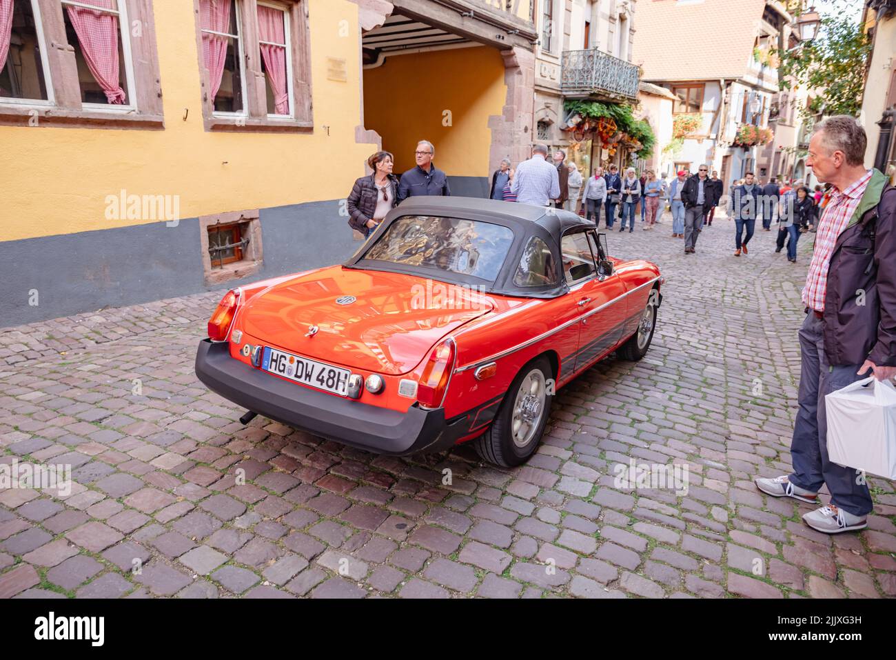 Red sports car drives through town with tourists onlooking Stock Photo ...