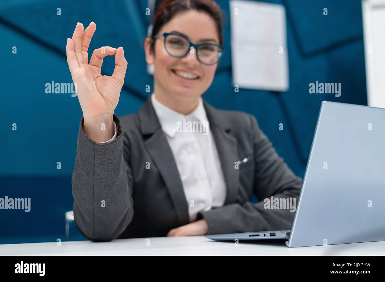 Business woman sitting at her desk and gesturing okay Stock Photo - Alamy