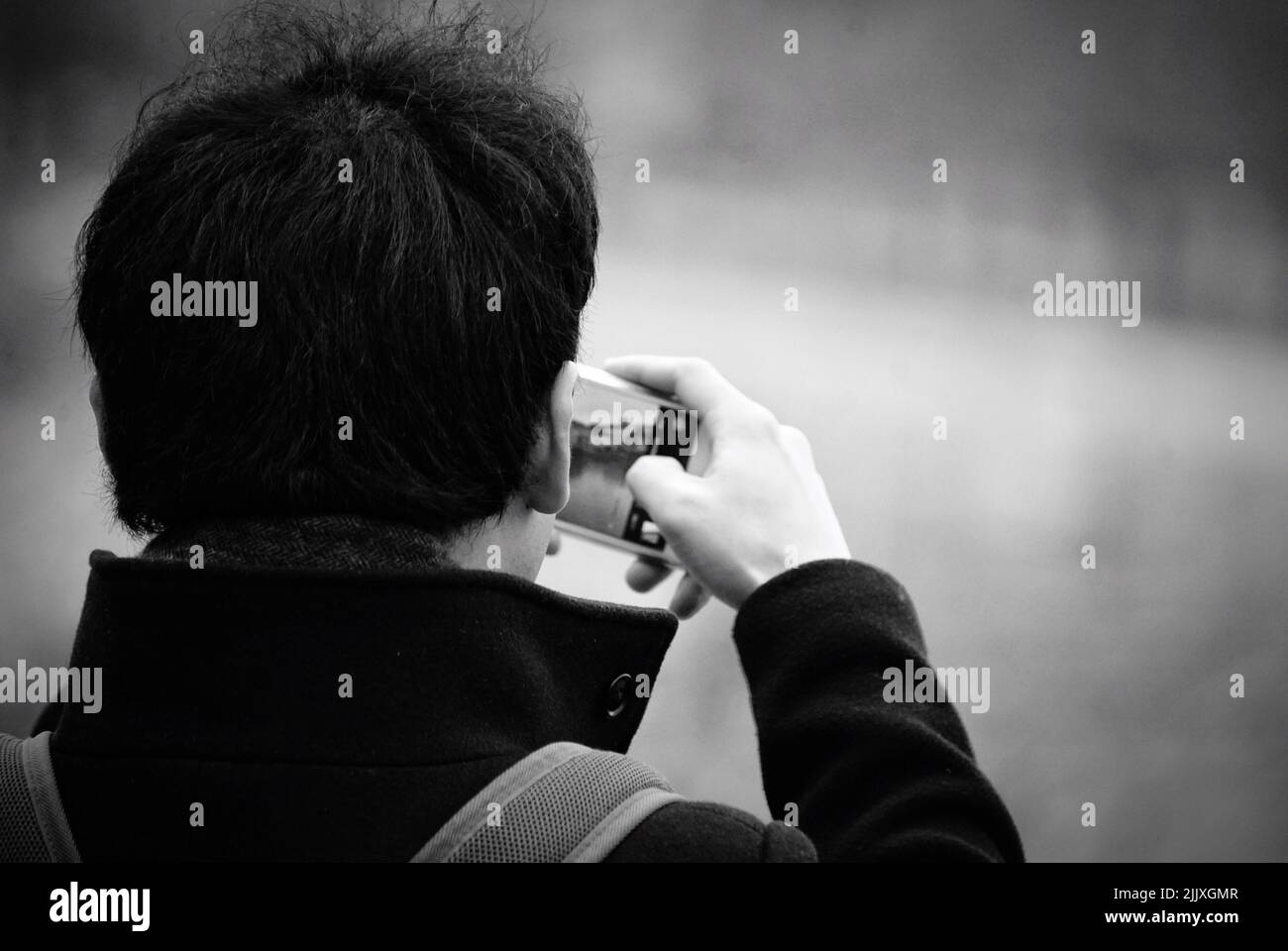 A close-up grayscale back view of a man taking a picture with his phone ...