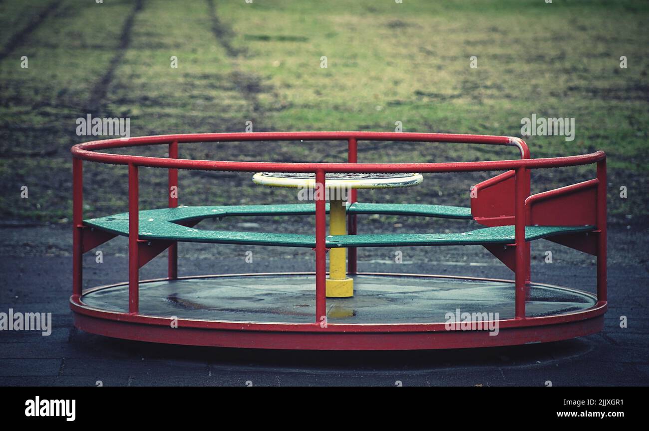 A red and green spinning carousel standing alone on the playground with ...