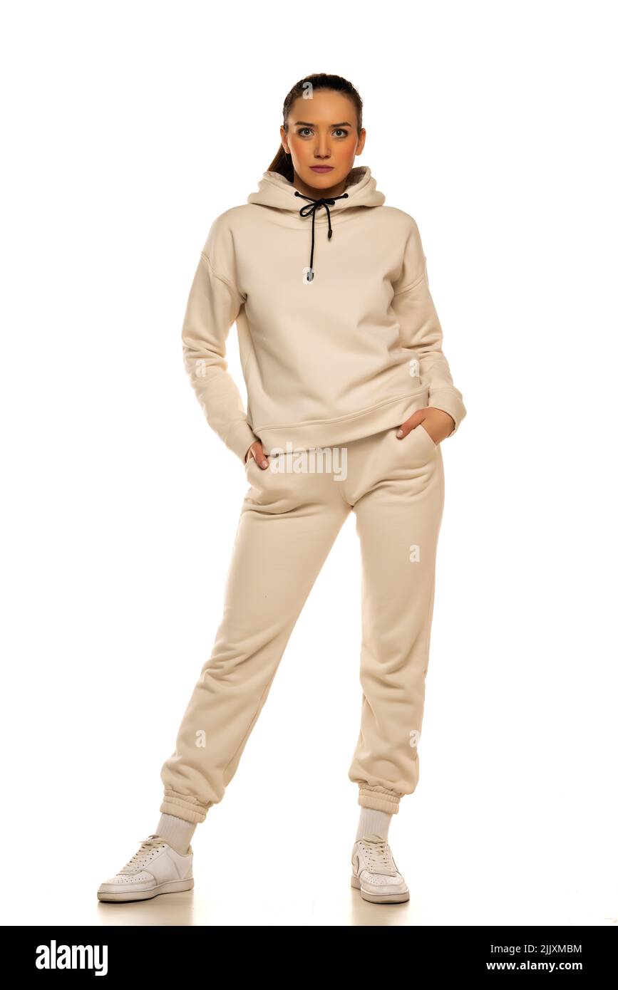 Front view of a young woman in a beige tracksuit posing to a white ...