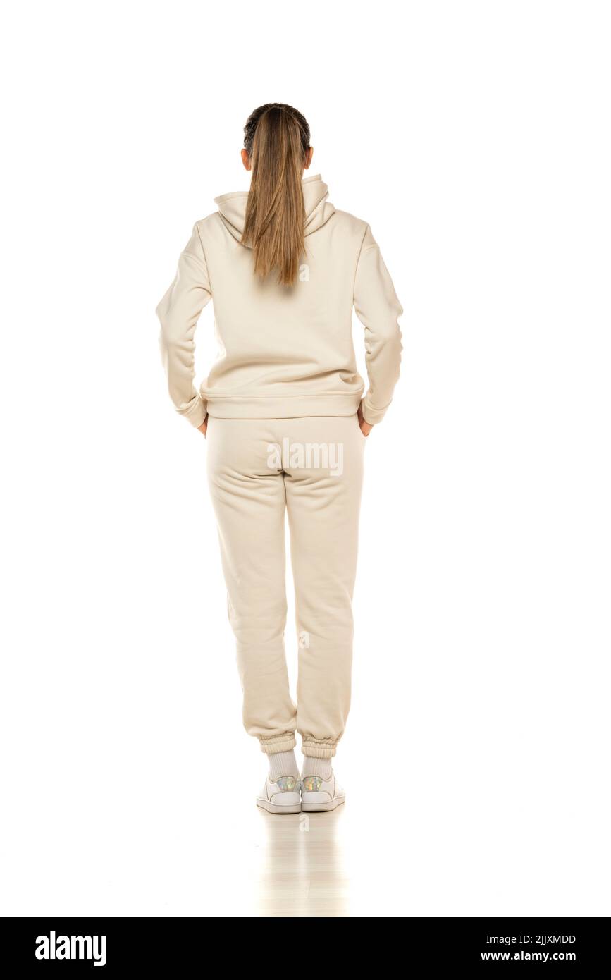 Rear view of a young woman in a beige tracksuit posing to a white ...