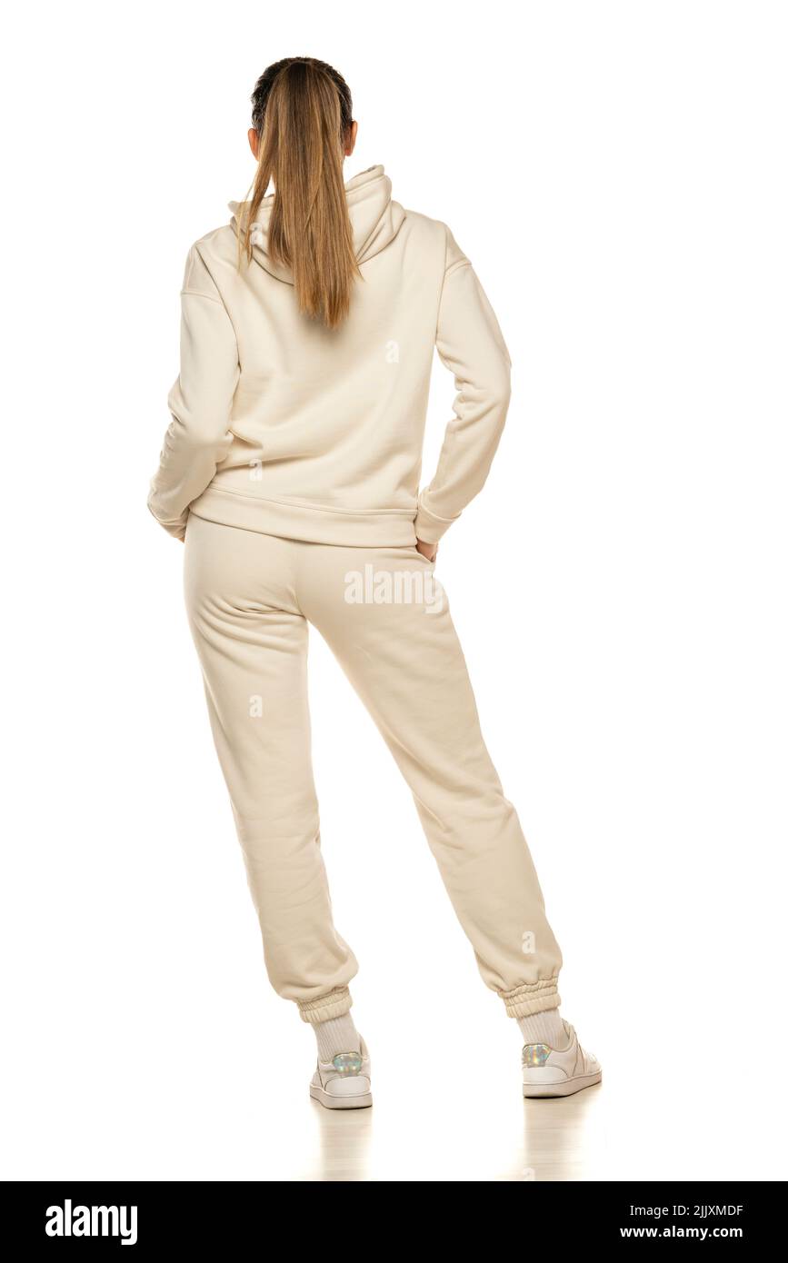 Rear view of a young woman in a beige tracksuit posing to a white ...
