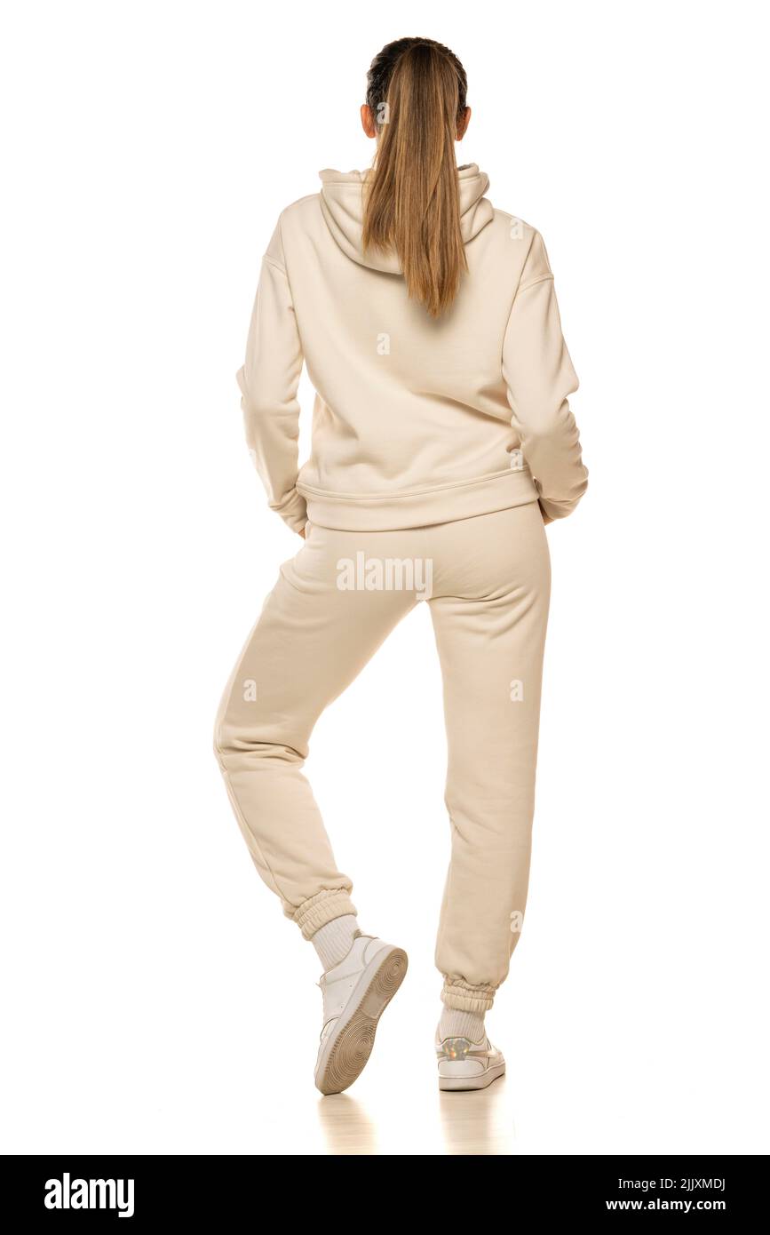Rear view of a young woman in a beige tracksuit posing to a white ...