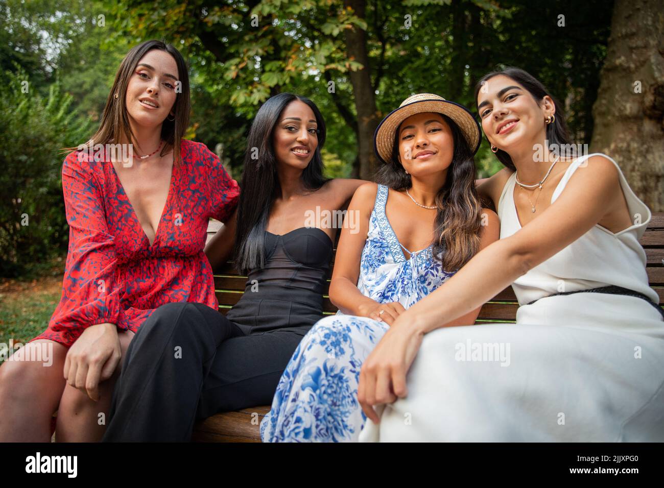 Four girl friends are sitting on a bench in a park in the open air ...