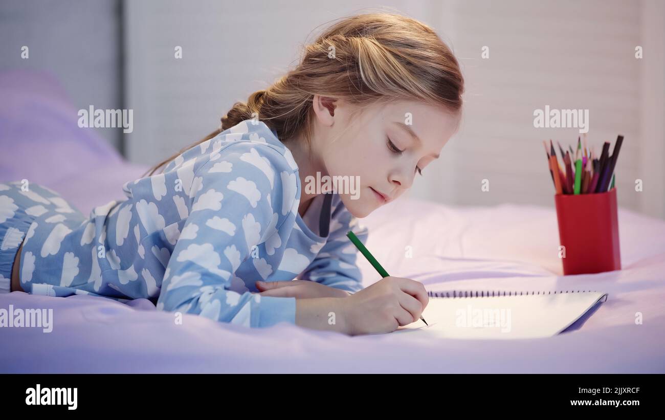 Preteen child drawing on sketchbook near color pencils on bed in ...