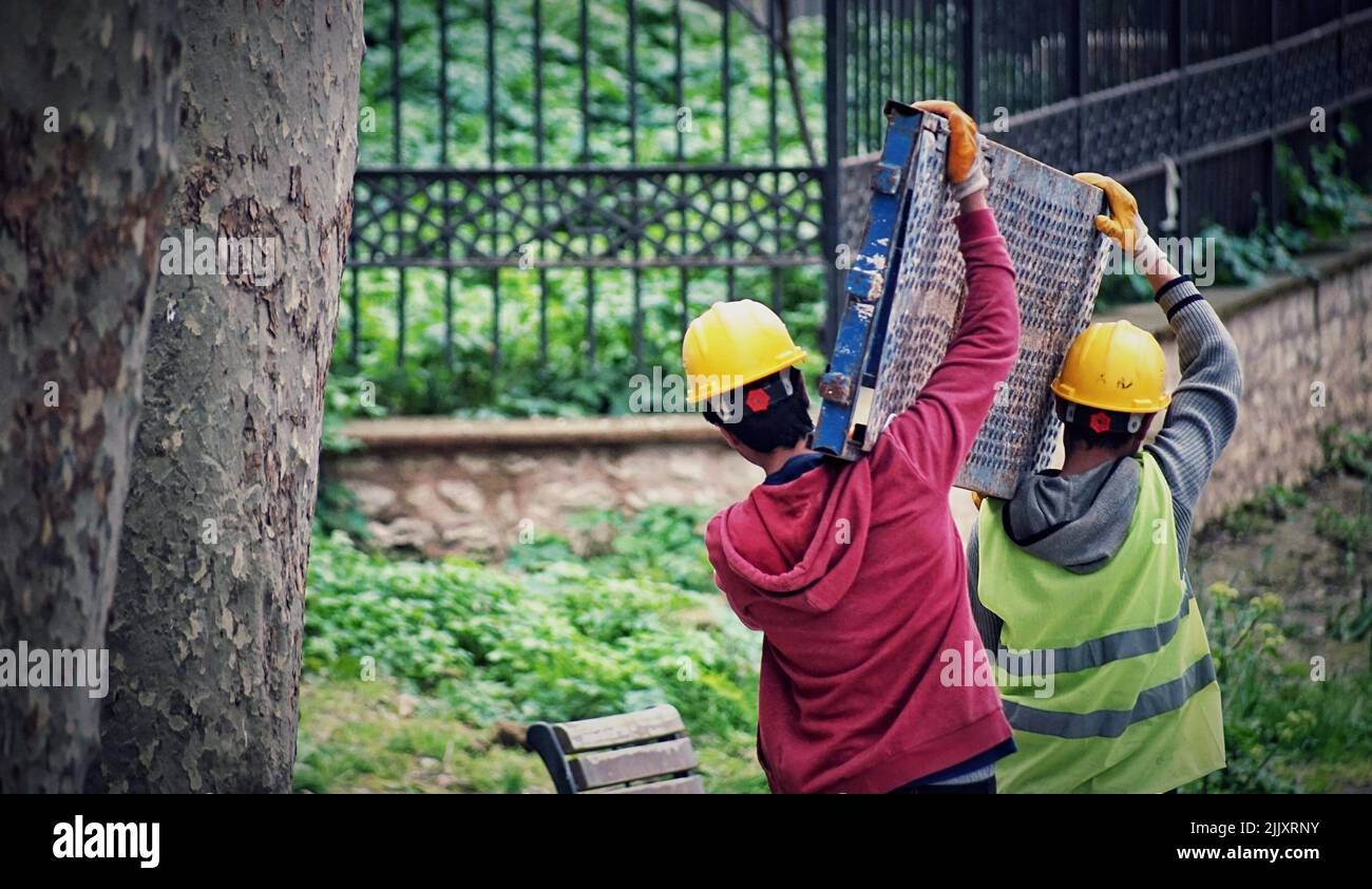 A pair of construction workers with helmets carrying heavy equipment ...