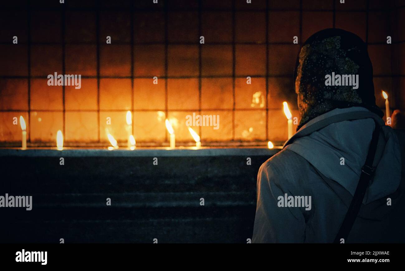 A back view of a person looking at a row of burning thin candles Stock ...