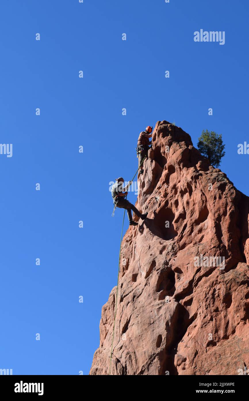 A vertical view of men climbing a red rock on a clear sunny day in ...