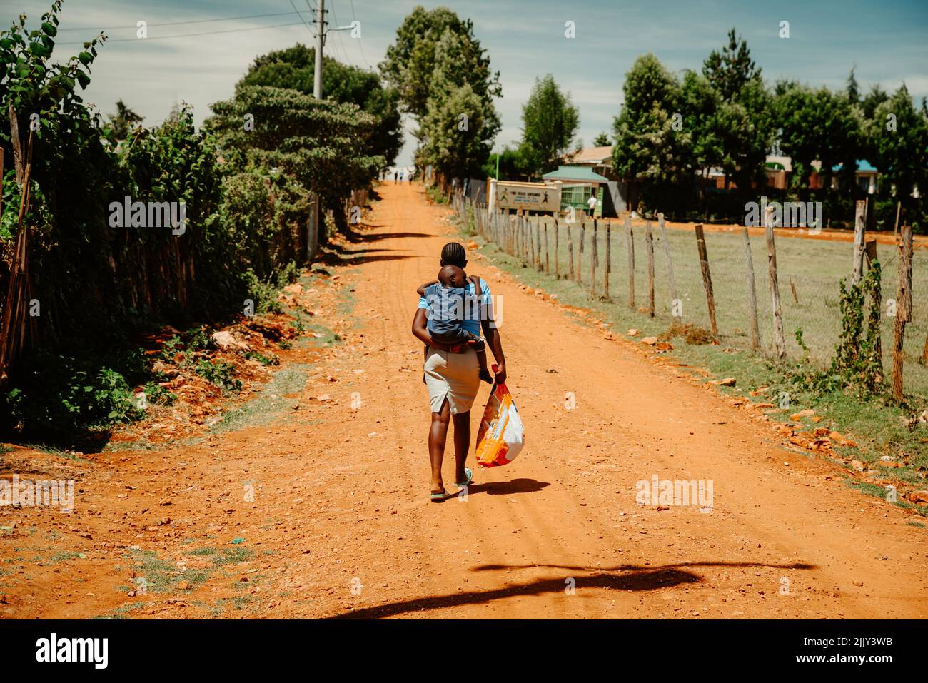A young African mother walks with her child on her shoulder ...