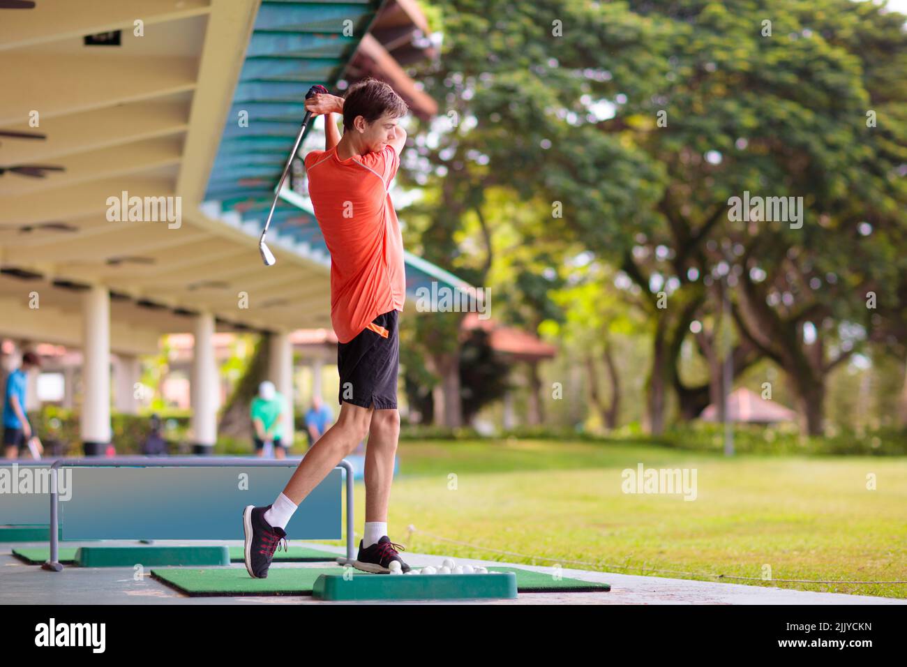 Young man hitting ball on golf driving range. Teenager exercising in ...