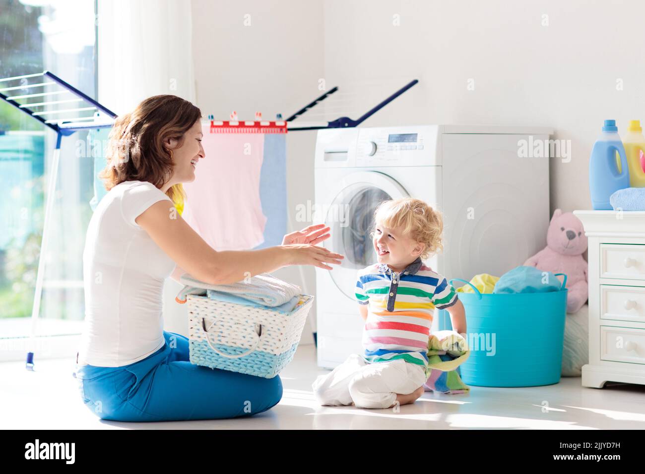Mother and kids in laundry room with washing machine or tumble dryer ...