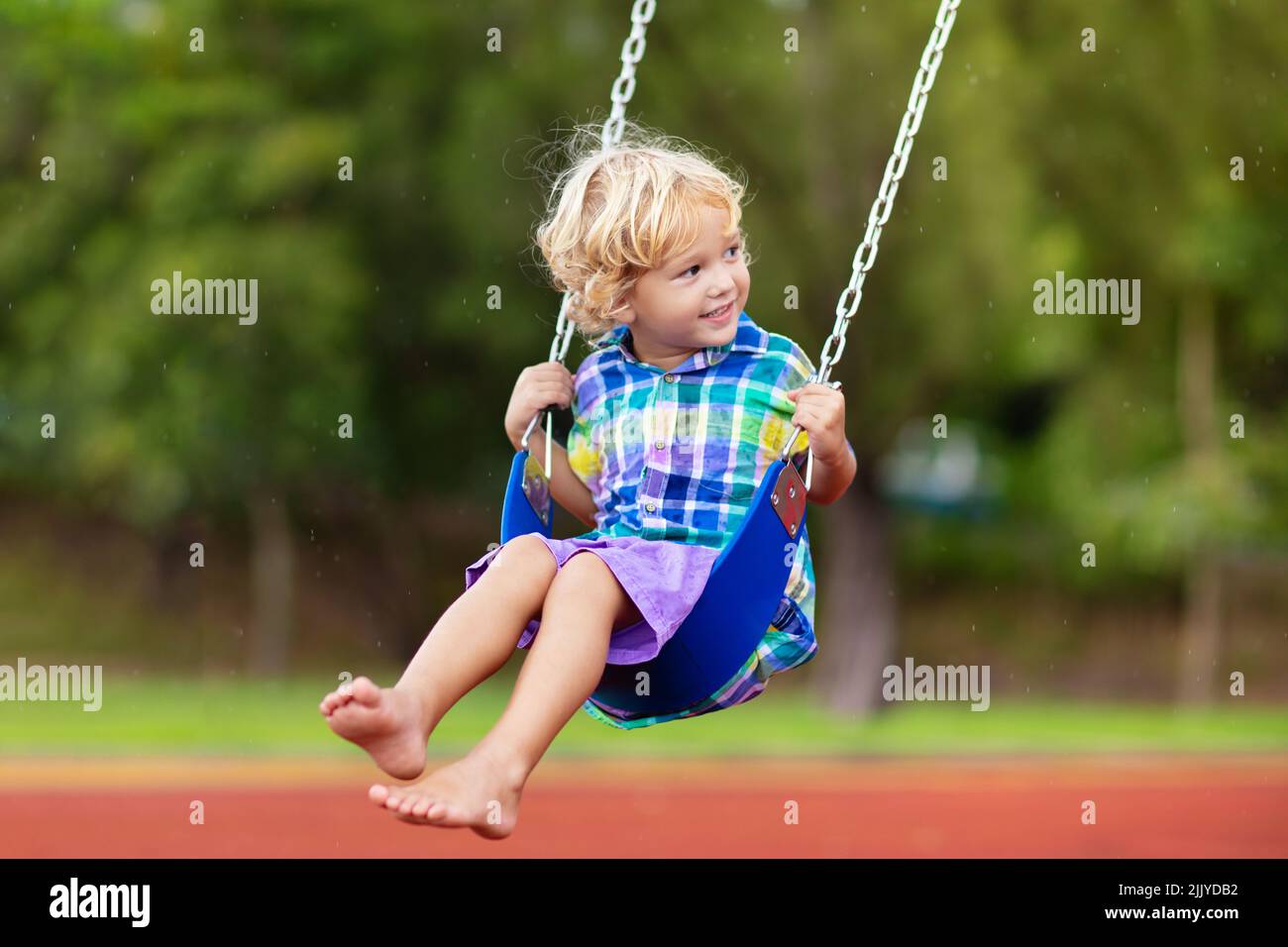 Child playing on outdoor playground in rain. Kids play on school or ...