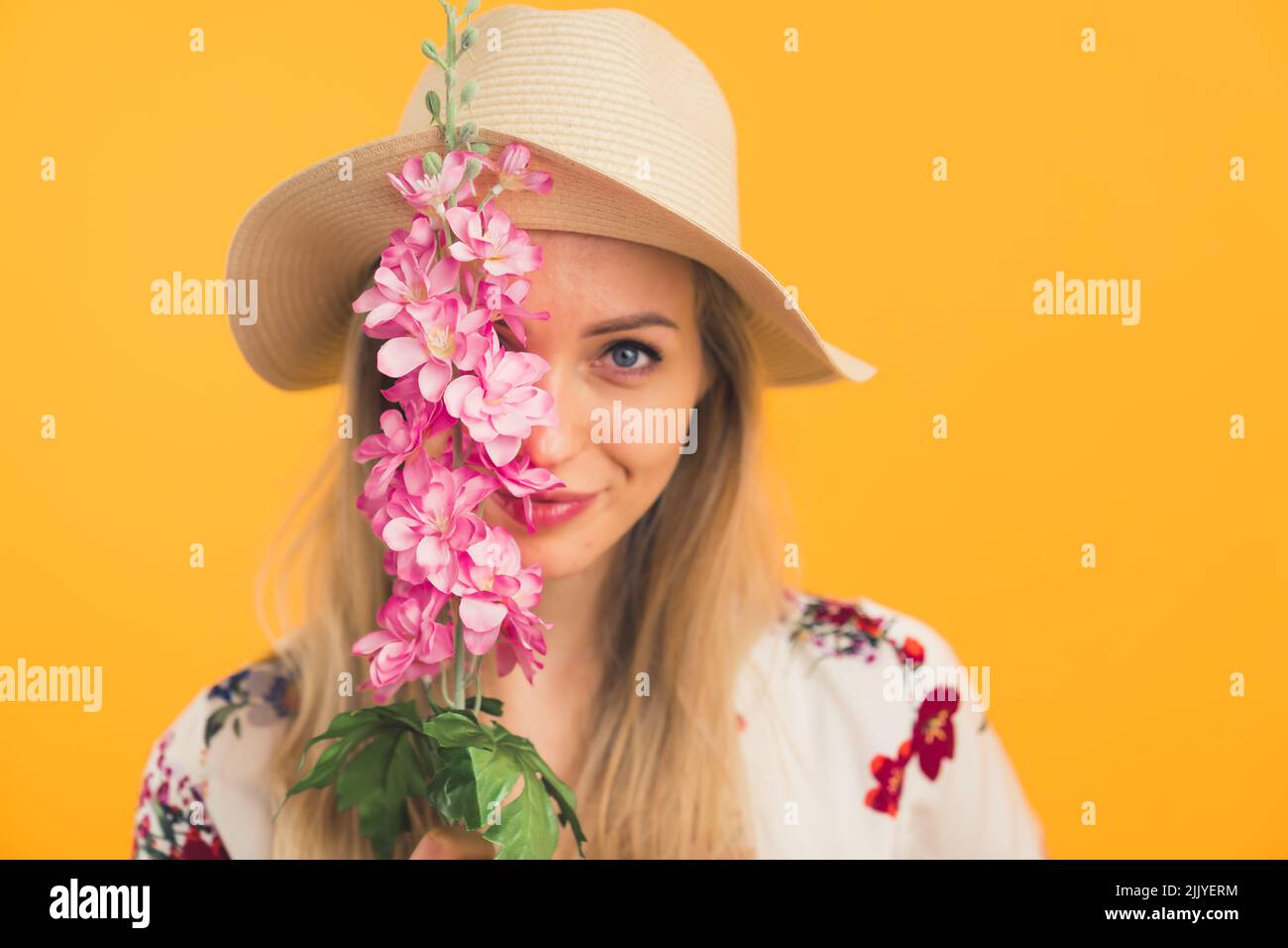 caucasian girl wearing a hat and holding a flower looking at the camera ...