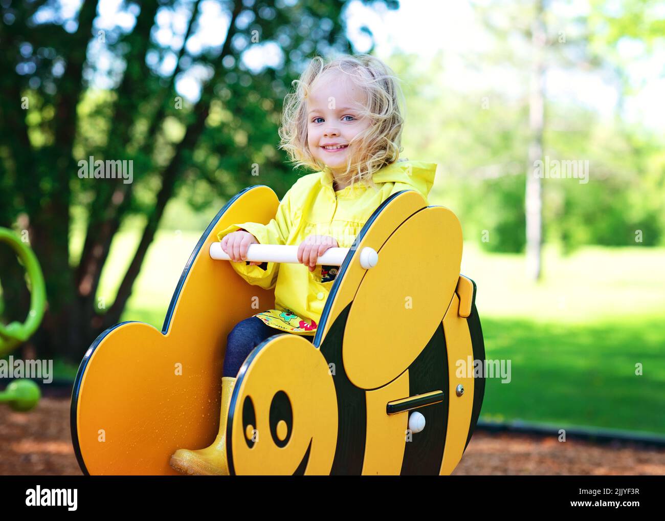 Blond toddler girl in yellow raincoat on bee ride, playground Stock ...