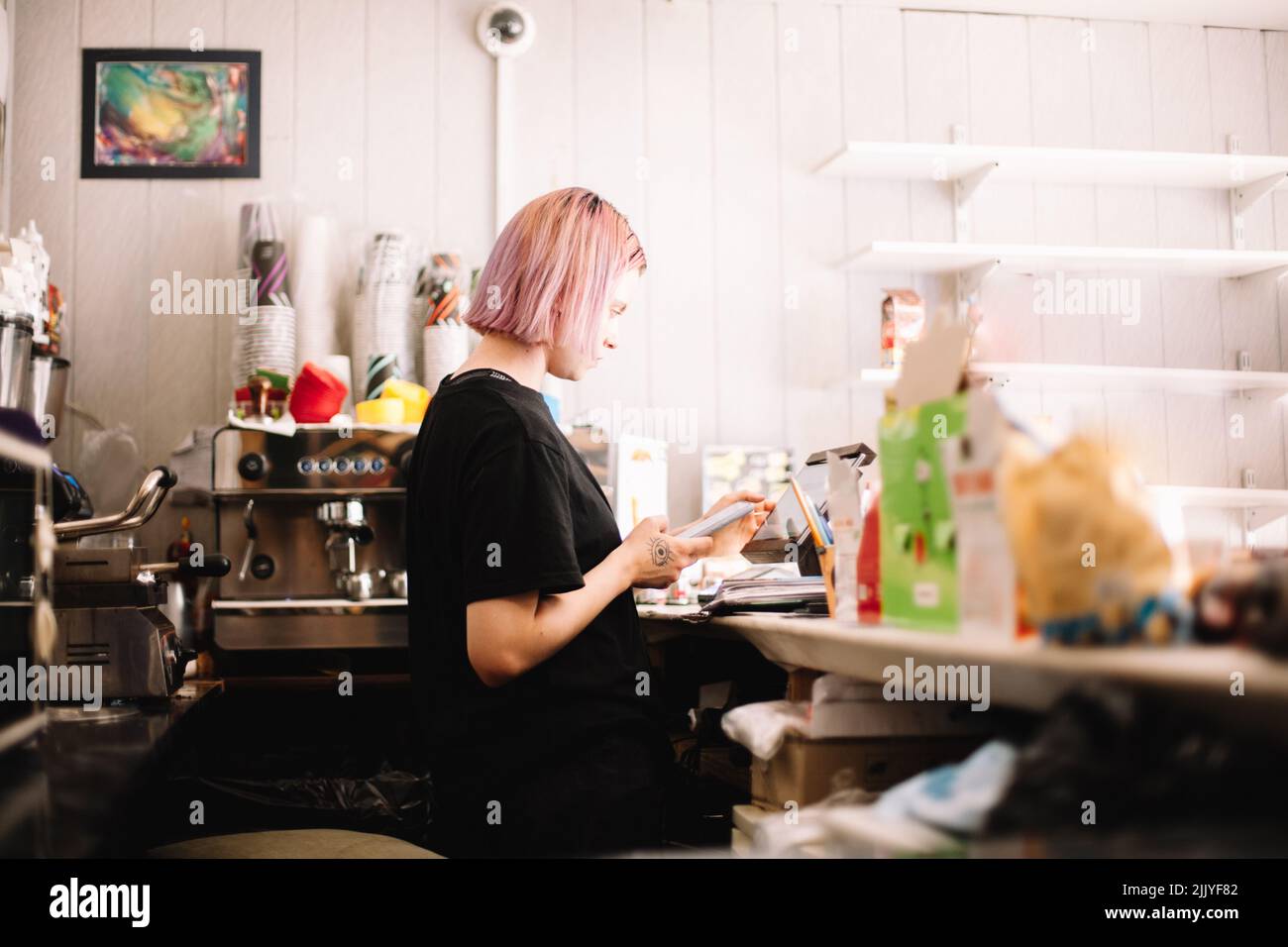 Female barista working at checkout counter on a tablet in coffee shop ...