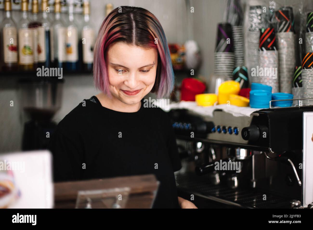 Happy young female barista standing at checkout counter in coffee shop ...