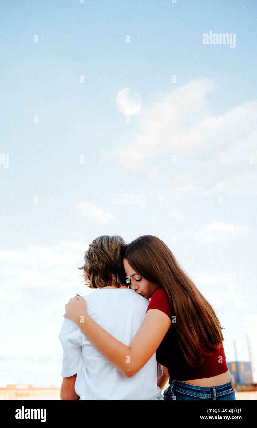 girlfriend kissing her boyfriend's shoulder as she embraces him Stock ...