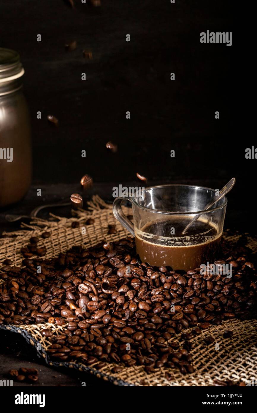 A vertical shot of a coffee in a glass cup surrounded by coffee beans ...
