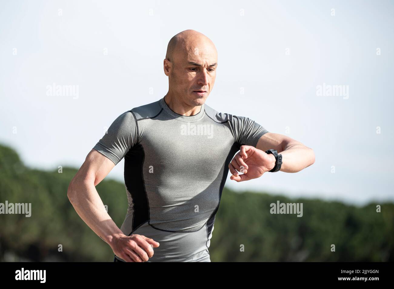 Man running in park at winter morning looking his watch Stock Photo - Alamy
