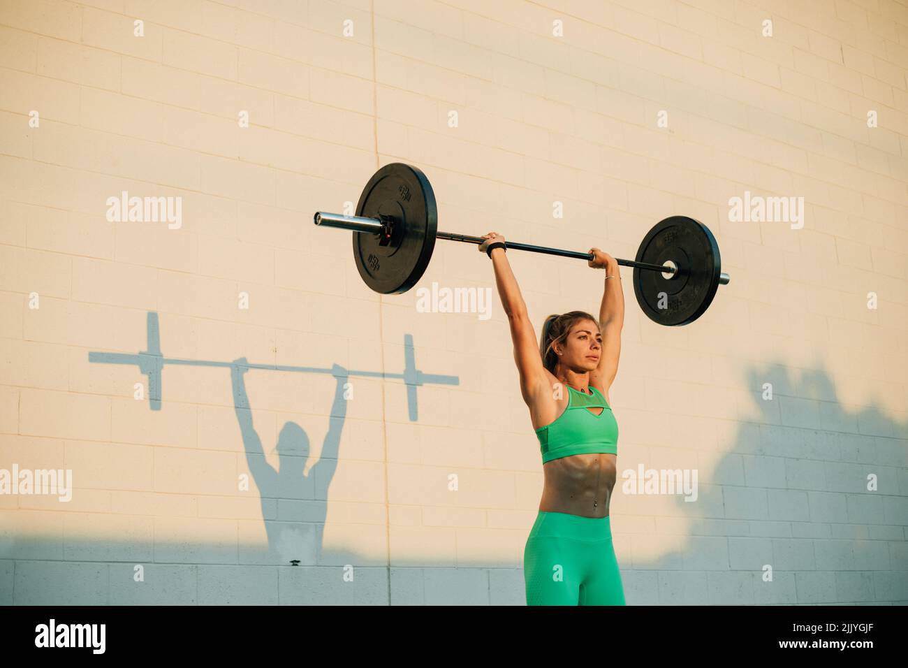 Young active woman doing overhead press with barbell in morning Stock ...