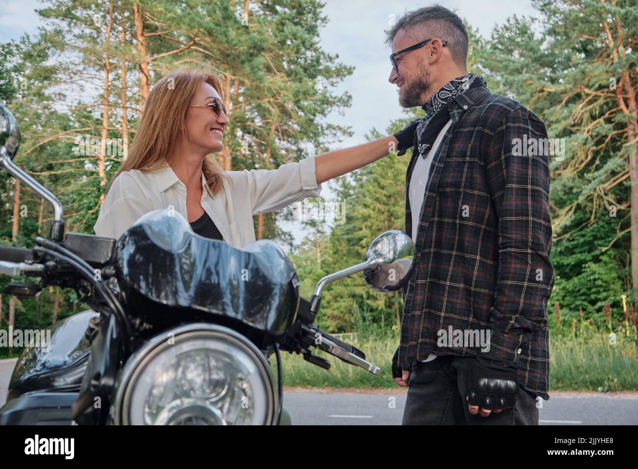 Middle age couple talking and having fun, sitting on a motorcycle, traveling together on a ...