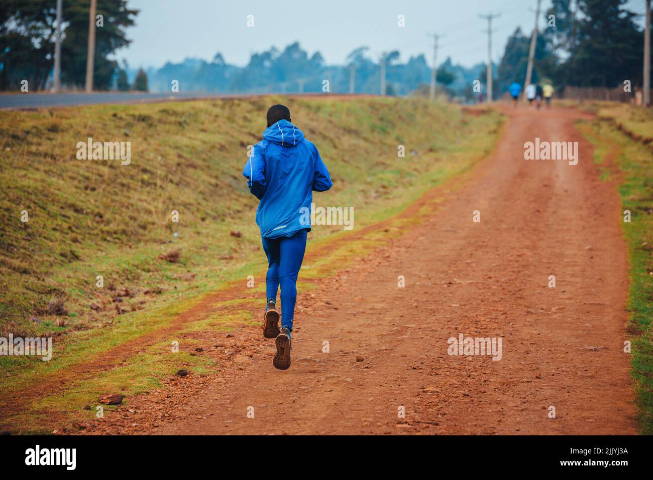A lone runner trains in Kenya. A marathon runner runs on red soil in ...