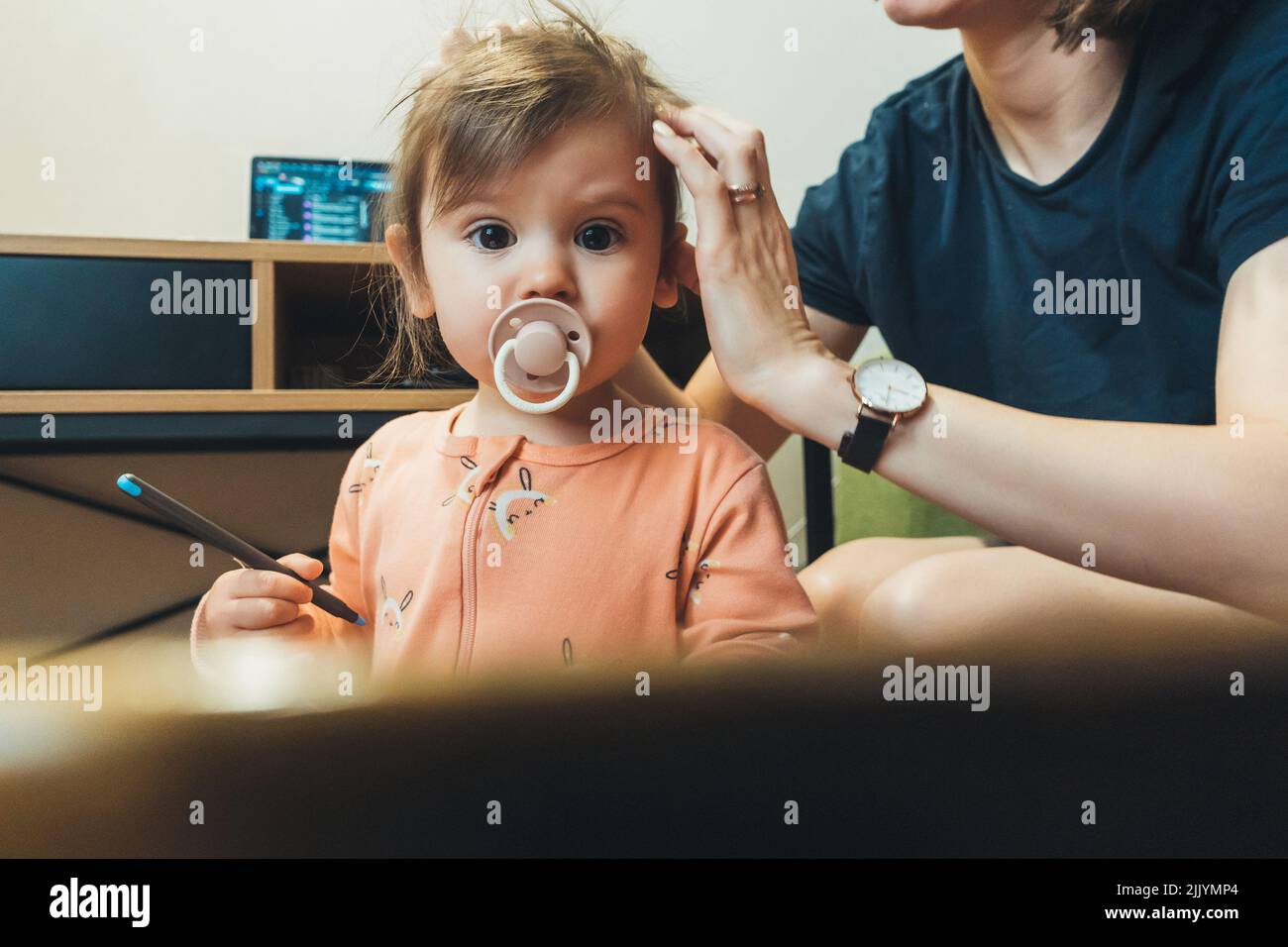 Curious baby girl looking with interest at camera, mother grooming baby ...