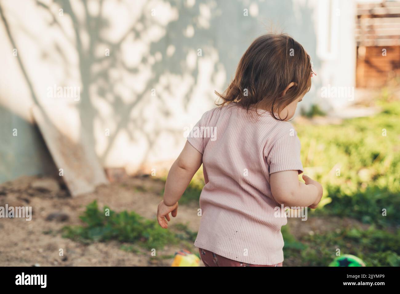 Rear view of a baby girl running through the yard of the house and ...