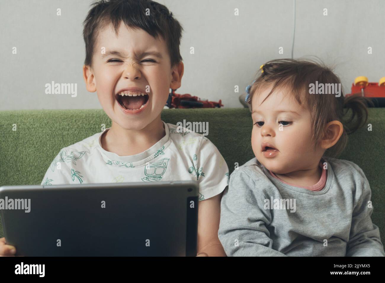 Two caucasian kids watching cartoons on tablet computer and laughing ...