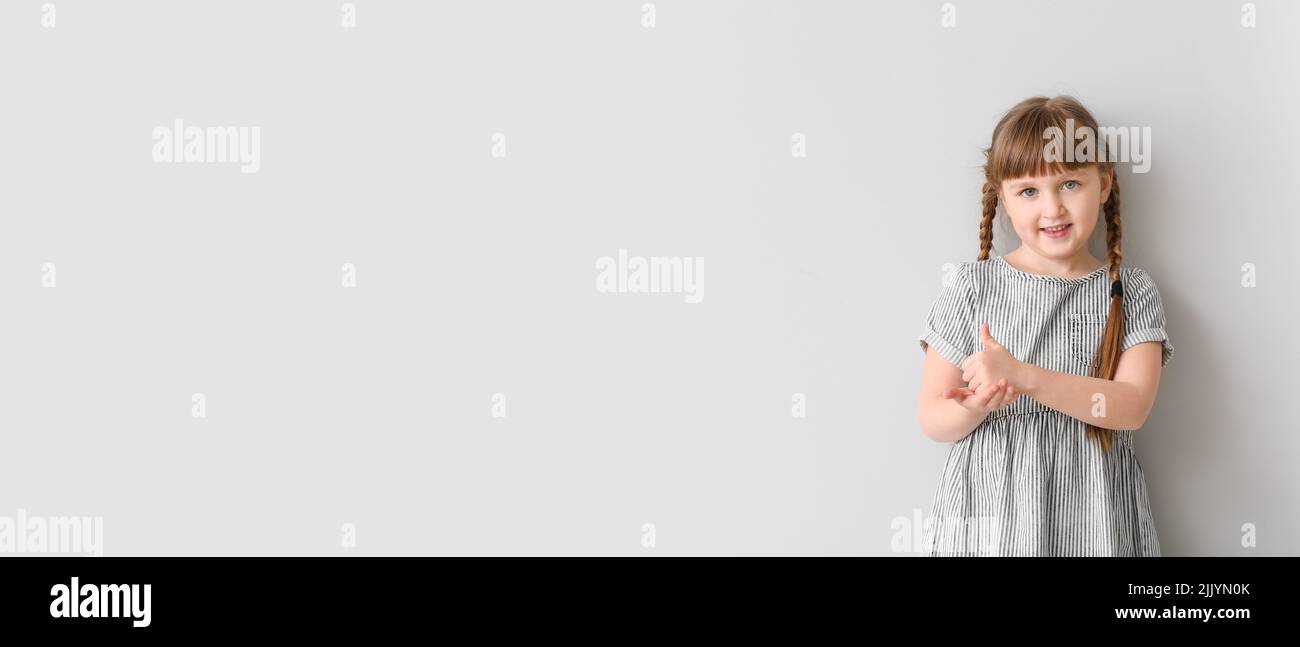 Little deaf mute girl using sign language on light background with ...