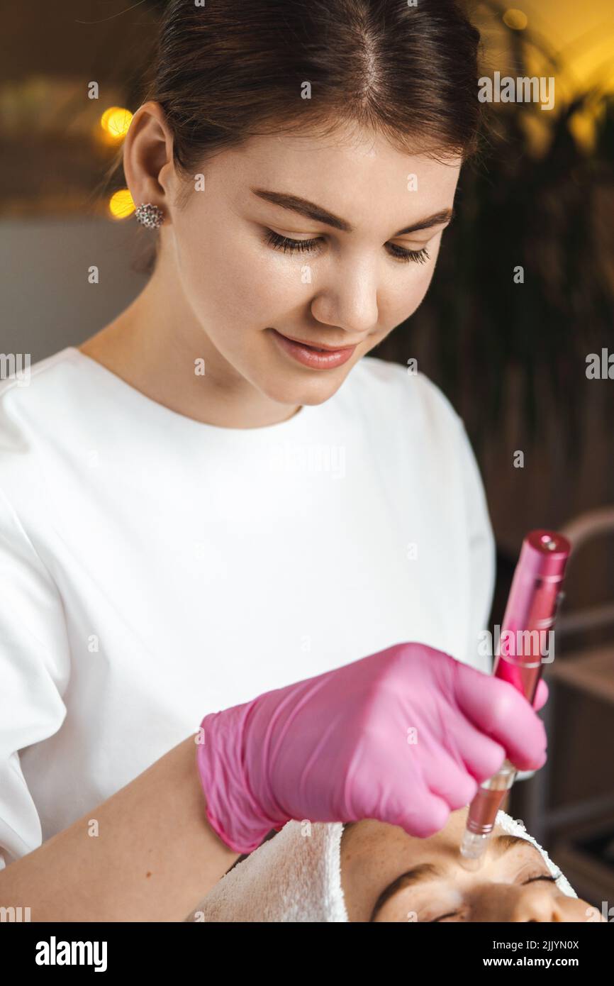 Professional woman cosmetologist doing procedure of microneedling with ...