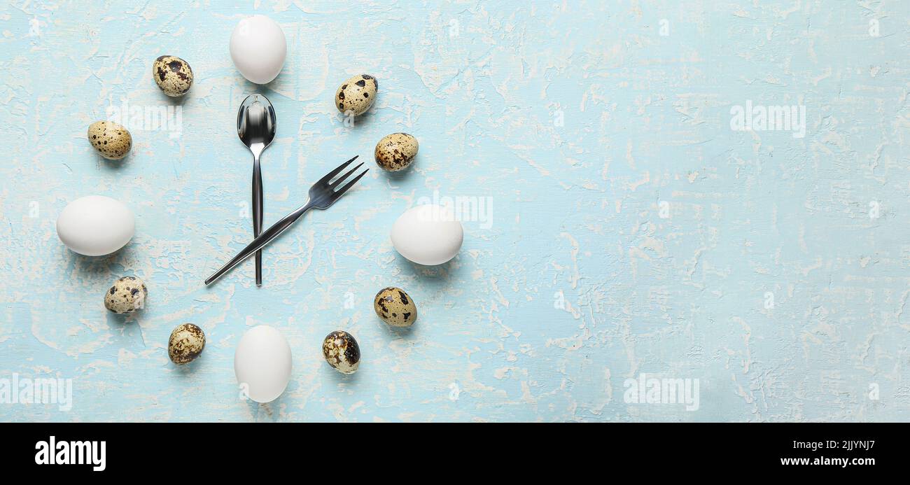 Clock made of eggs and cutlery on light blue background with space for ...