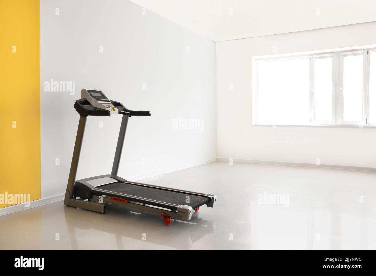 Modern treadmill near yellow and white wall Stock Photo - Alamy