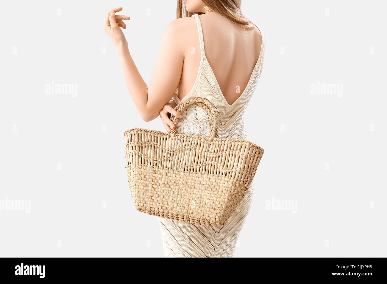 Elegant woman in dress holding rattan handbag behind her back on light ...