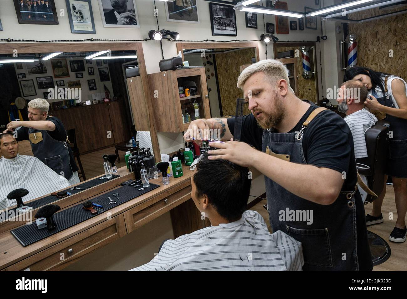 Hairstylists give haircuts to customers at a re-opened barbershop ...